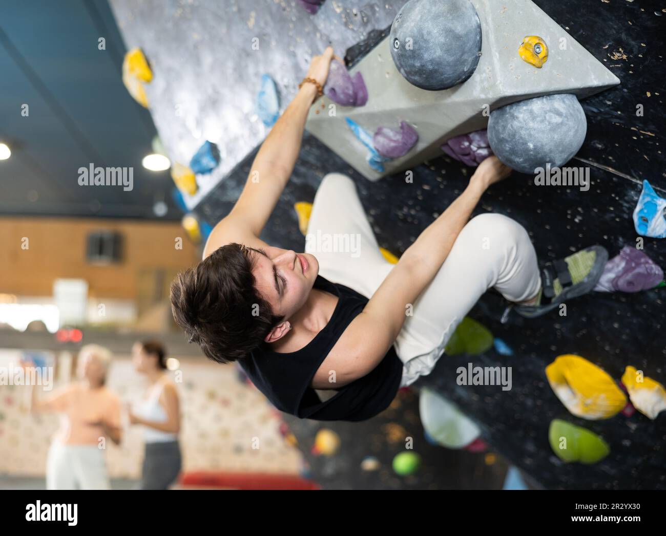 young muscular male sportsman climbing black wall for bouldering in gym ...