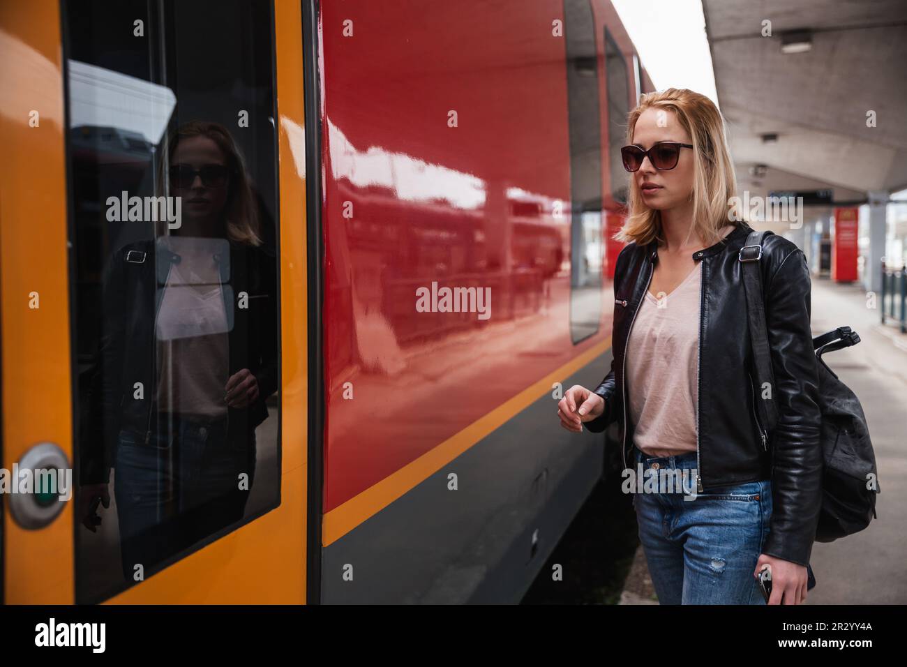 Young blond woman in jeans, shirt and leather jacket wearing bag and ...