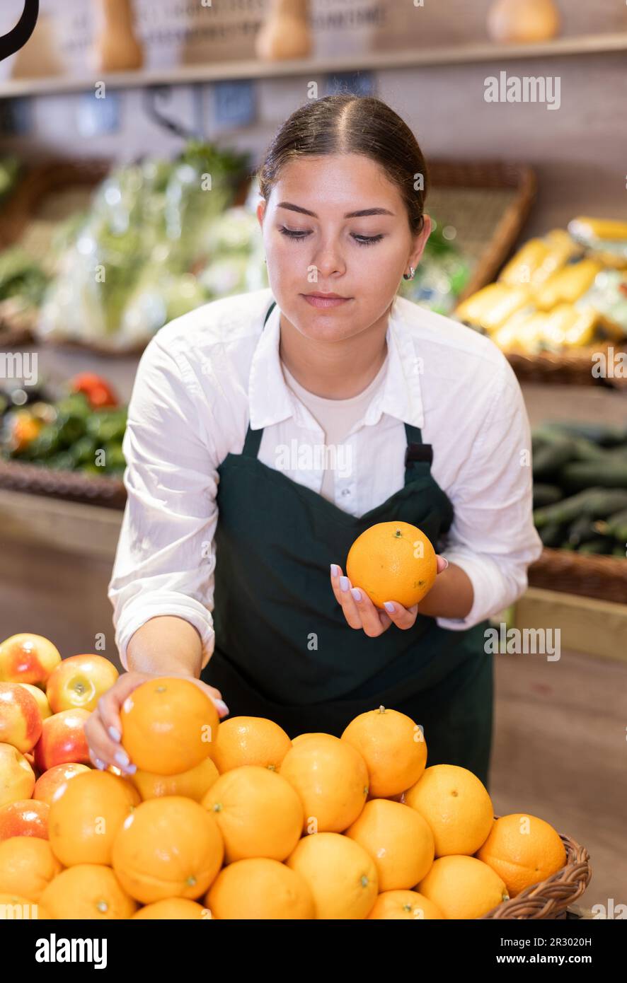 Female grocery store worker lays out ripe oranges on counter and ...