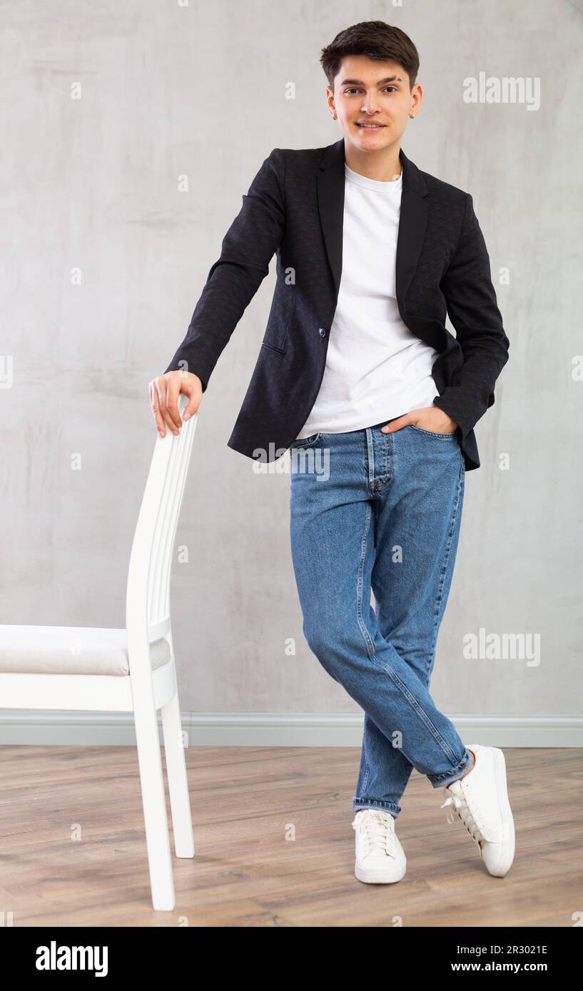 Smiling young man standing next to chair in the middle of the room ...