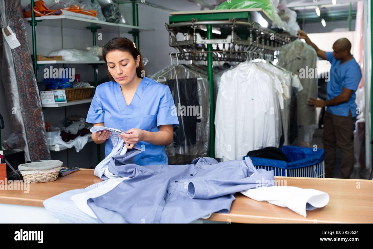 Focused woman dry-cleaning worker checking clean clothes Stock Photo ...