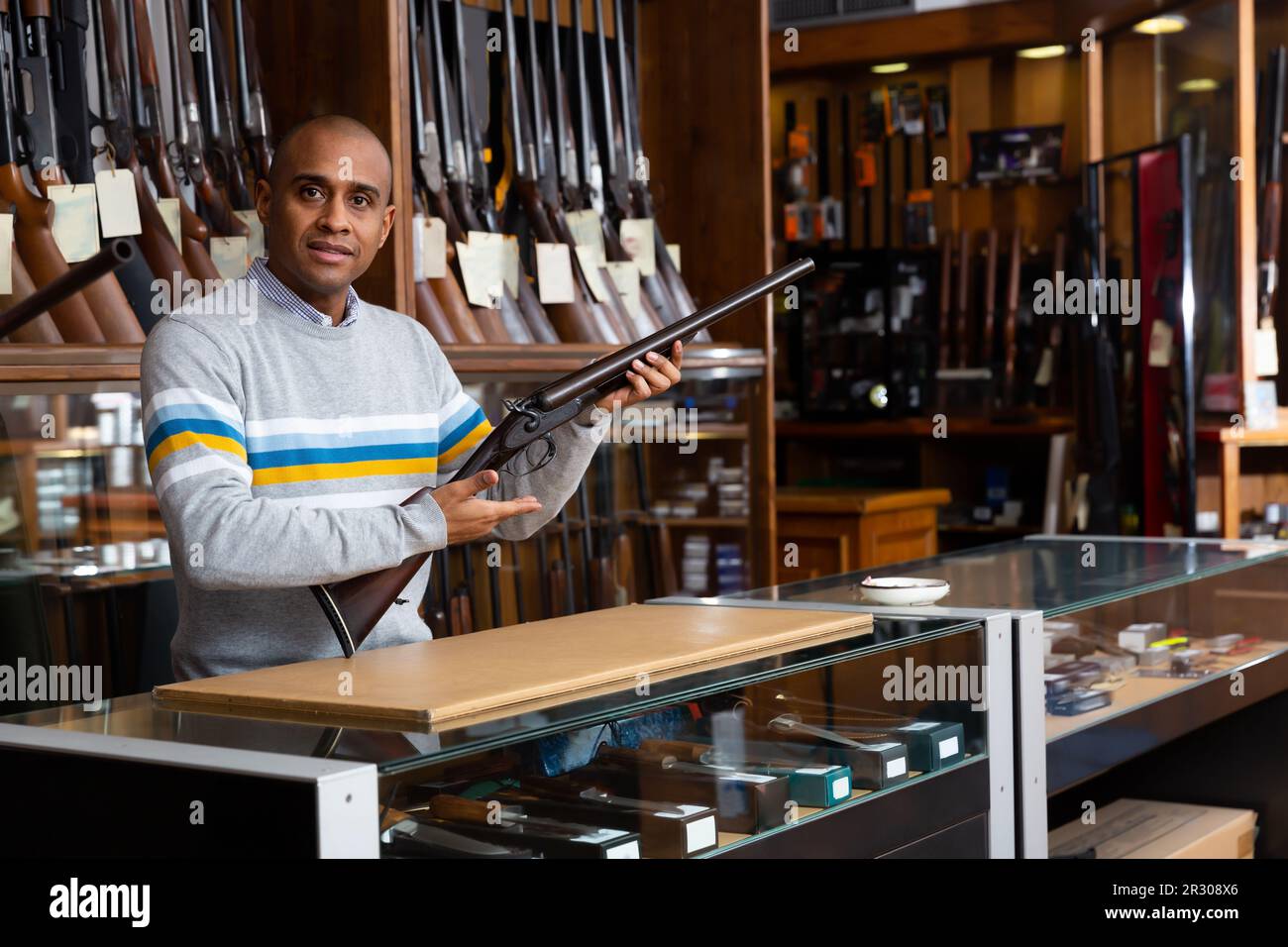 Portrait of male standing with rare collectible rifle in hunting shop ...