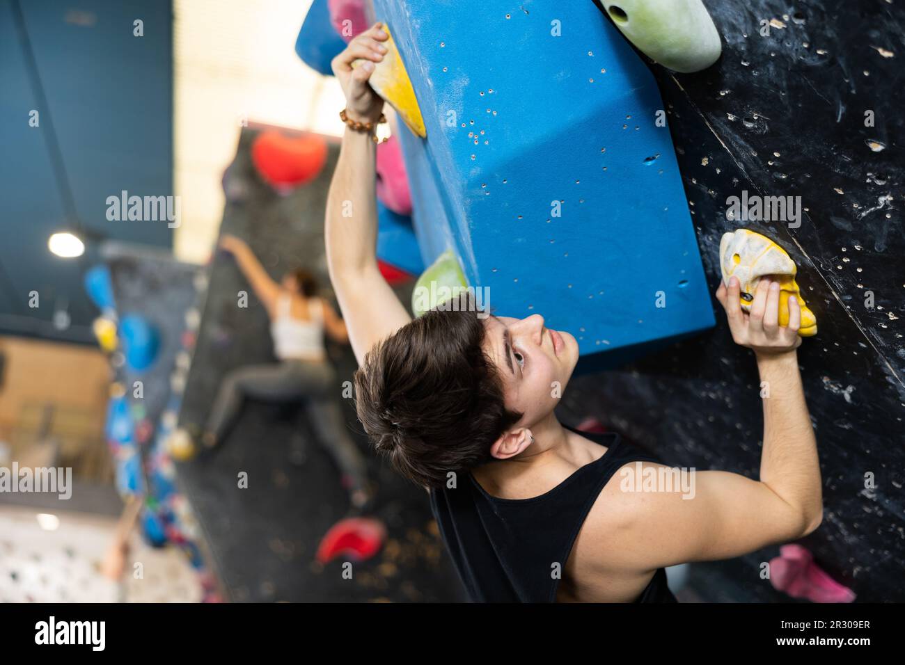 young muscular male sportsman climbing black wall for bouldering in gym ...