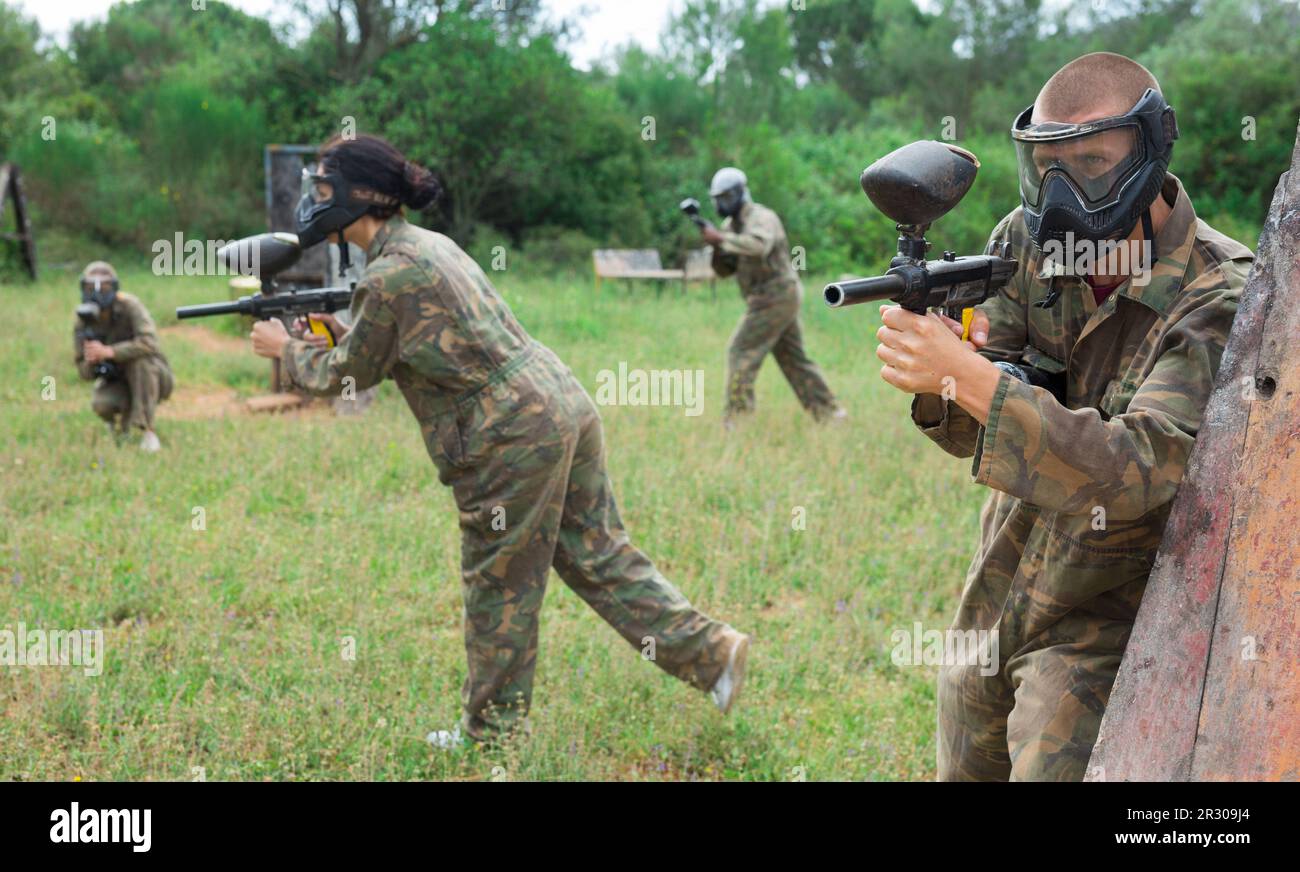 Excited male and female paintball players in protective uniform aiming ...