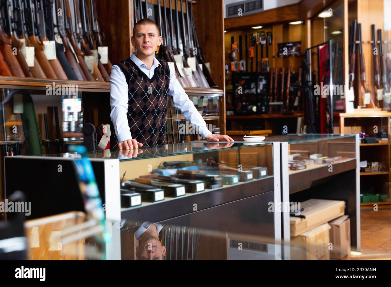Confident owner of gun shop standing behind counter Stock Photo - Alamy