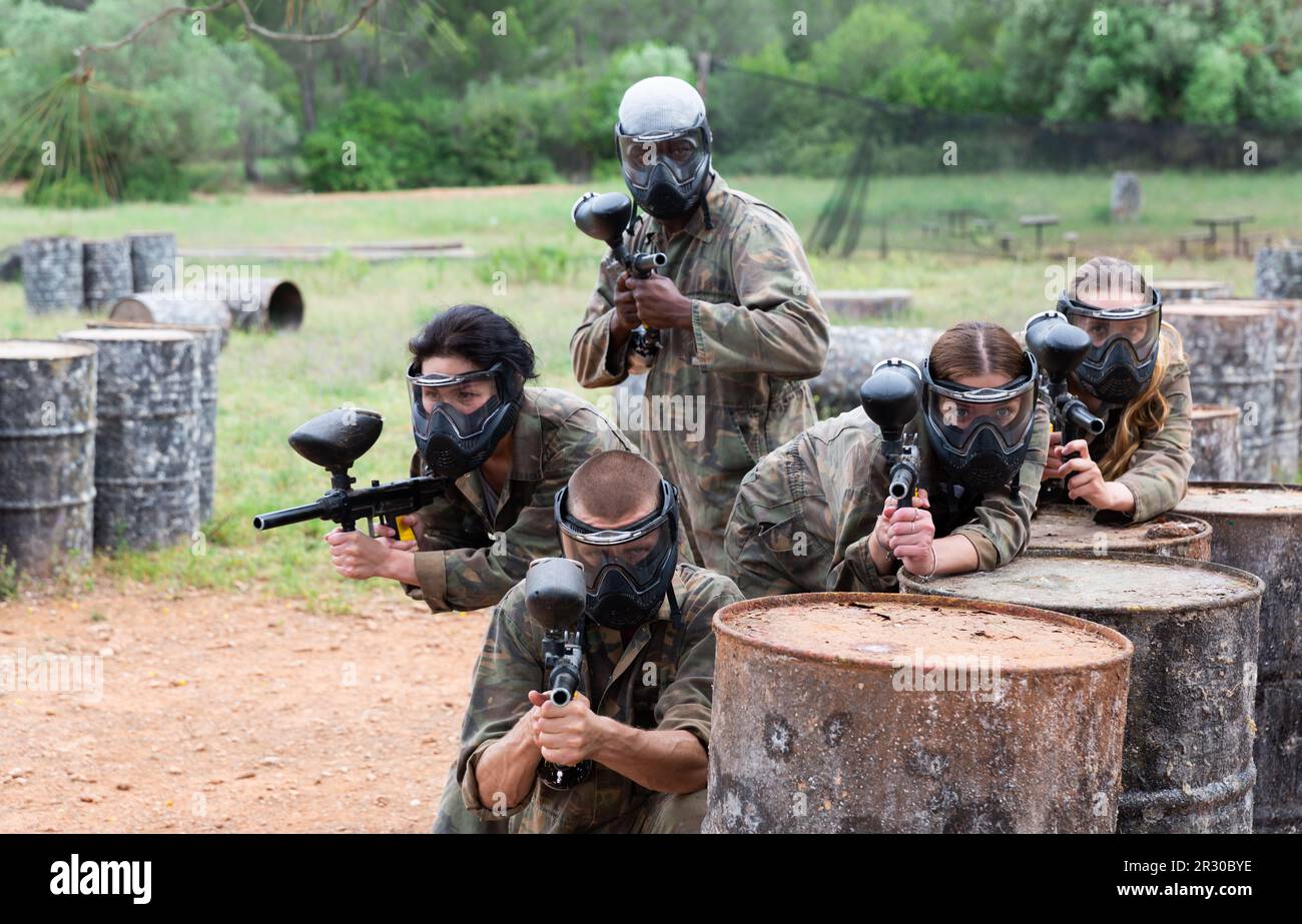 Excited male and female paintball players in protective uniform aiming ...