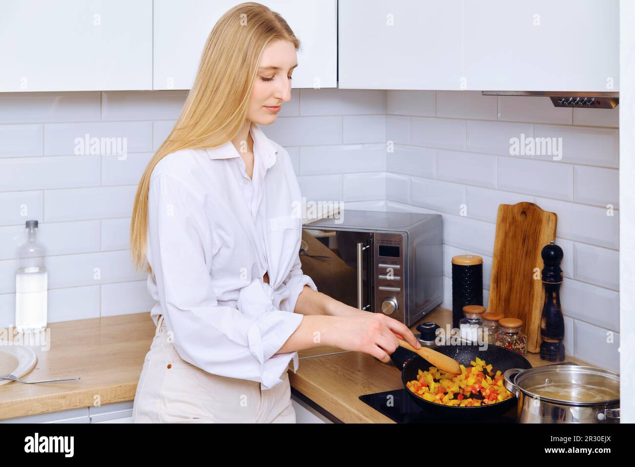 Cute woman is mixing vegetables in a frying pan Stock Photo - Alamy