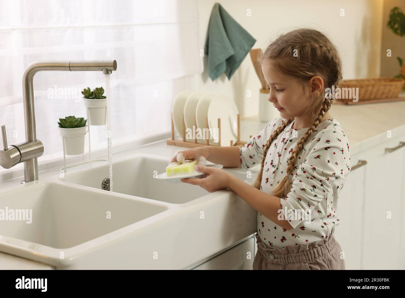 Little girl washing plate above sink in kitchen Stock Photo - Alamy