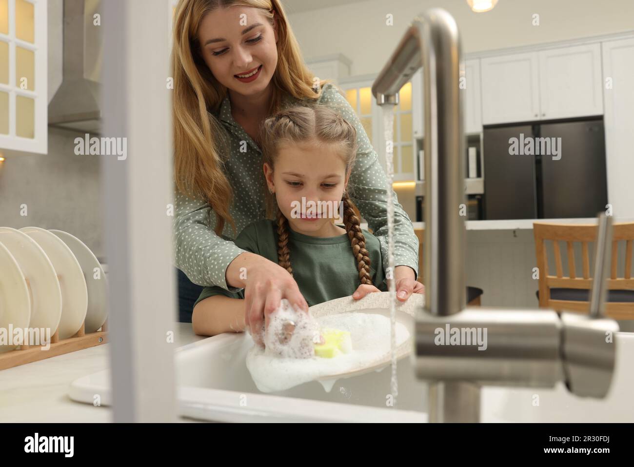 Mother and daughter washing plate above sink in kitchen, view from ...