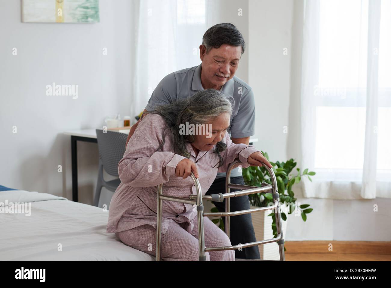 Elderly woman trying to get up from bed leaning on walker Stock Photo ...