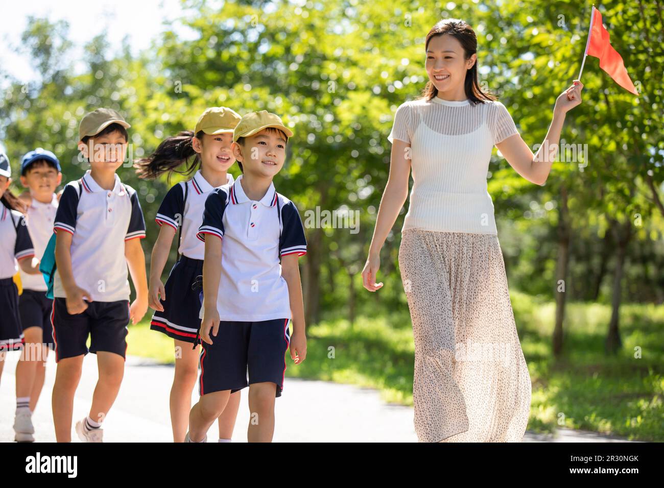 Cheerful Chinese school children walking in park with their teacher ...