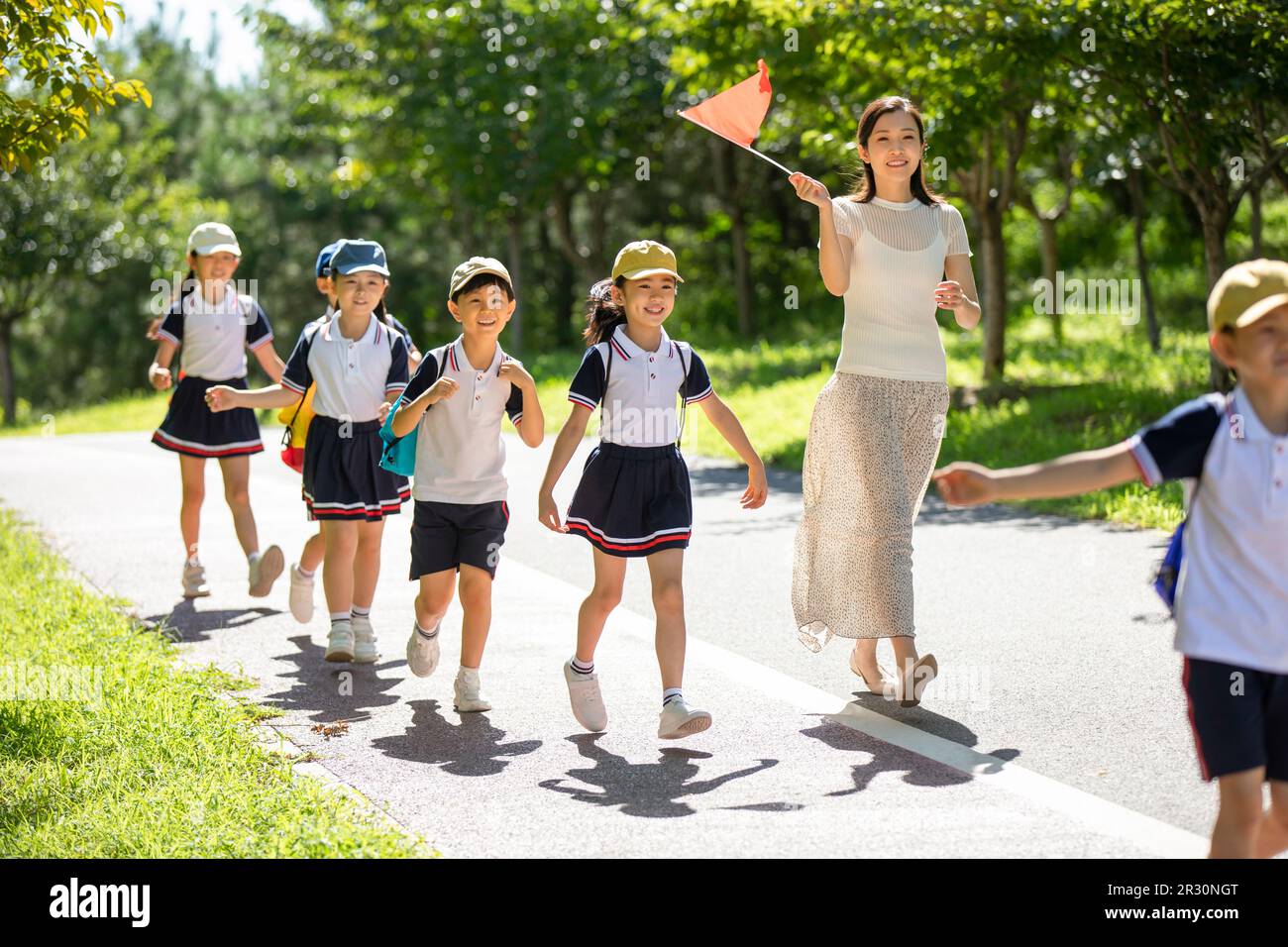 Cheerful Chinese school children walking in park with their teacher ...