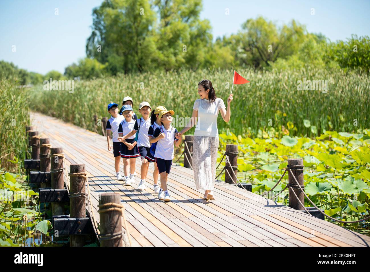 Cheerful Chinese school children walking in park with their teacher ...