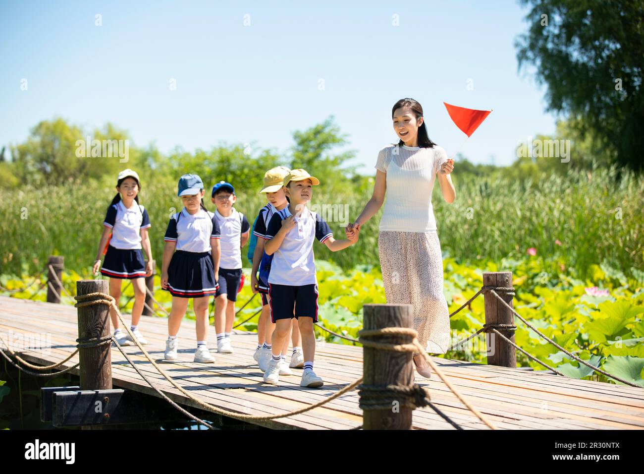 Cheerful Chinese school children walking in park with their teacher ...