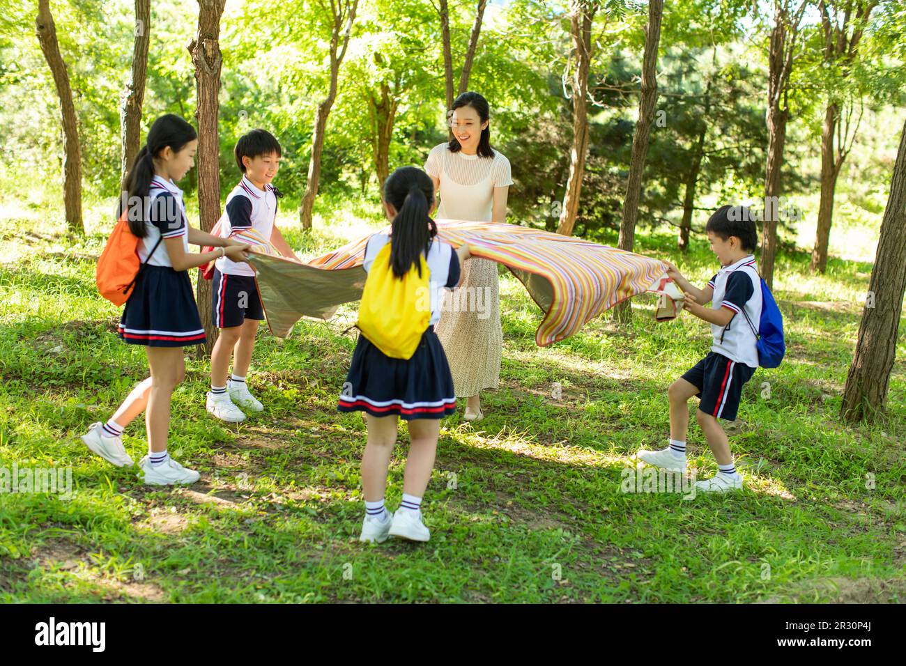 Cheerful Chinese school children picnicking outdoors with their teacher ...
