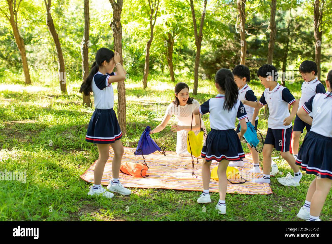 Cheerful Chinese school children picnicking outdoors with their teacher ...