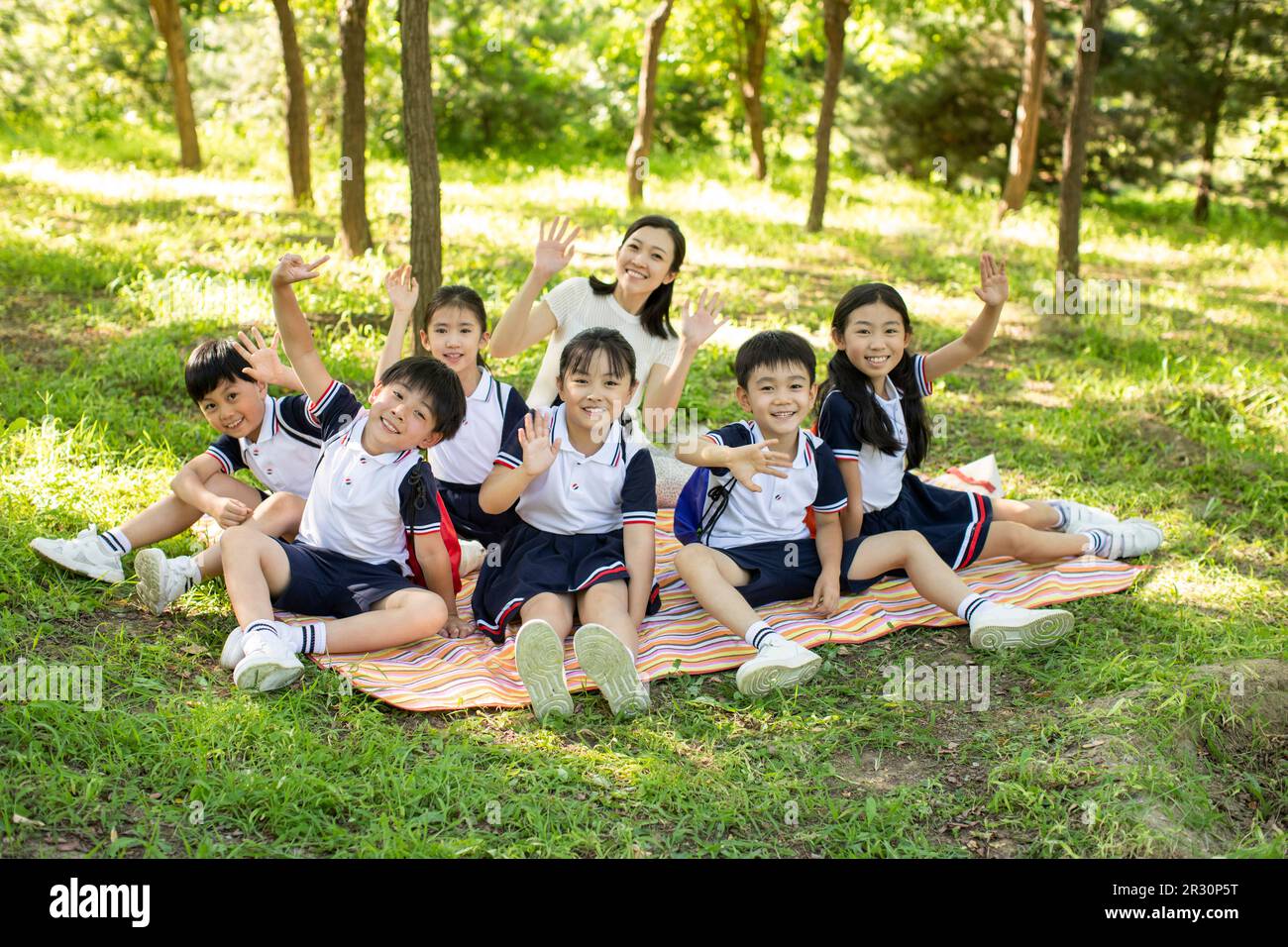 Cheerful Chinese school children picnicking outdoors with their teacher ...