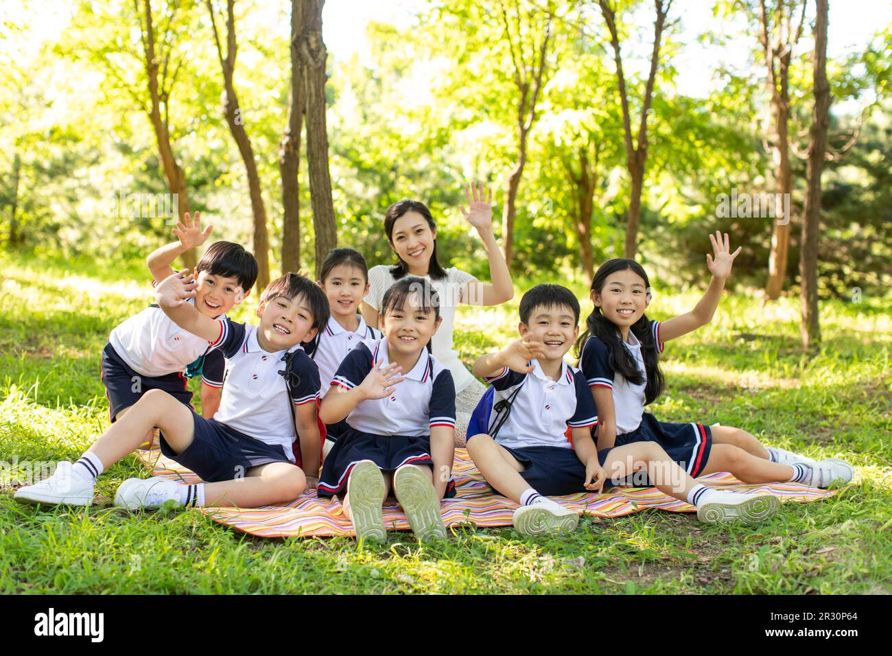 Cheerful Chinese school children picnicking outdoors with their teacher ...