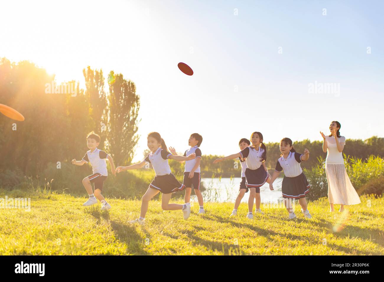 Cheerful Chinese school children playing frisbees with their teacher in ...