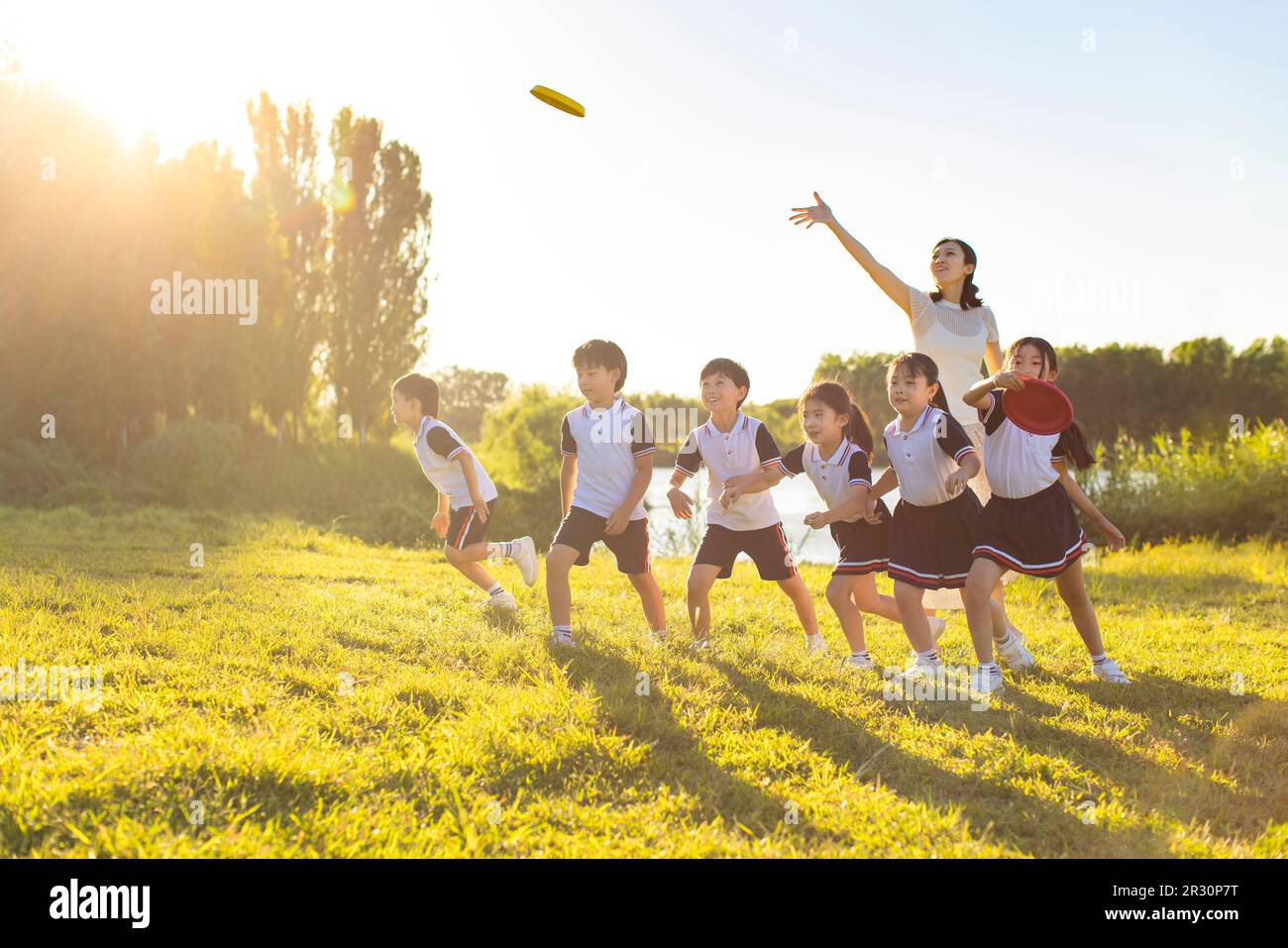 Cheerful Chinese school children playing frisbees with their teacher in ...