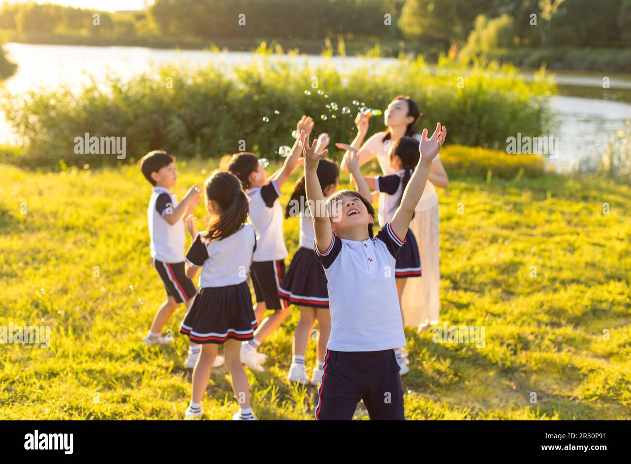 Cheerful Chinese school children and their teacher blowing bubbles on ...