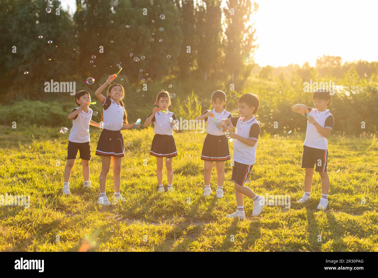 Cheerful Chinese school children blowing bubbles on meadow Stock Photo ...