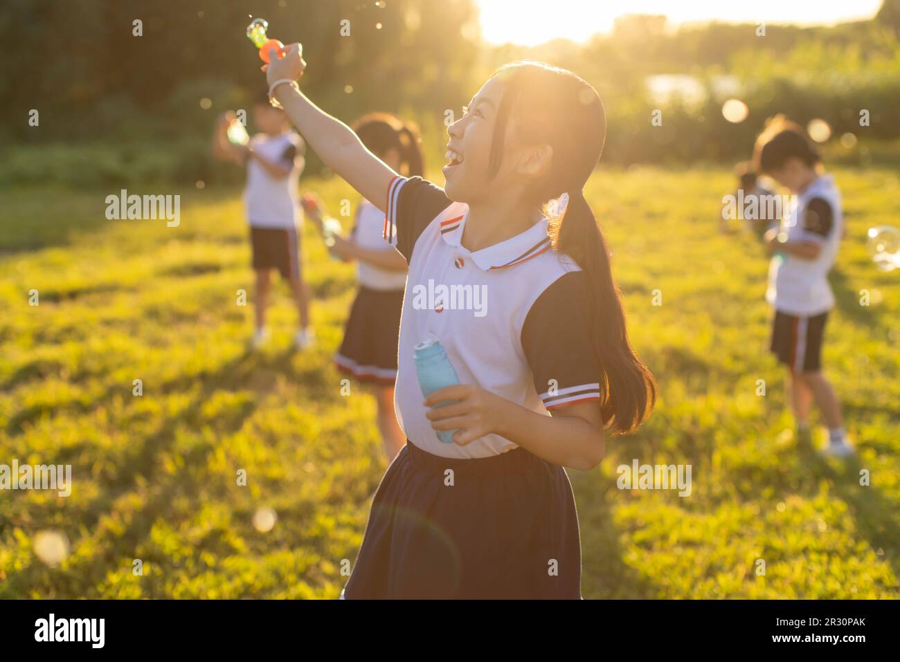 Cheerful Chinese school children blowing bubbles on meadow Stock Photo ...