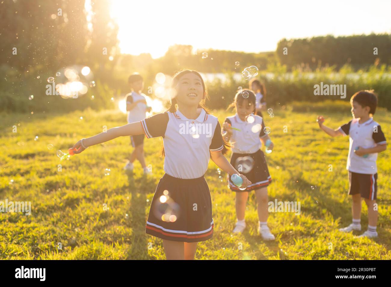 Cheerful Chinese school children blowing bubbles on meadow Stock Photo ...