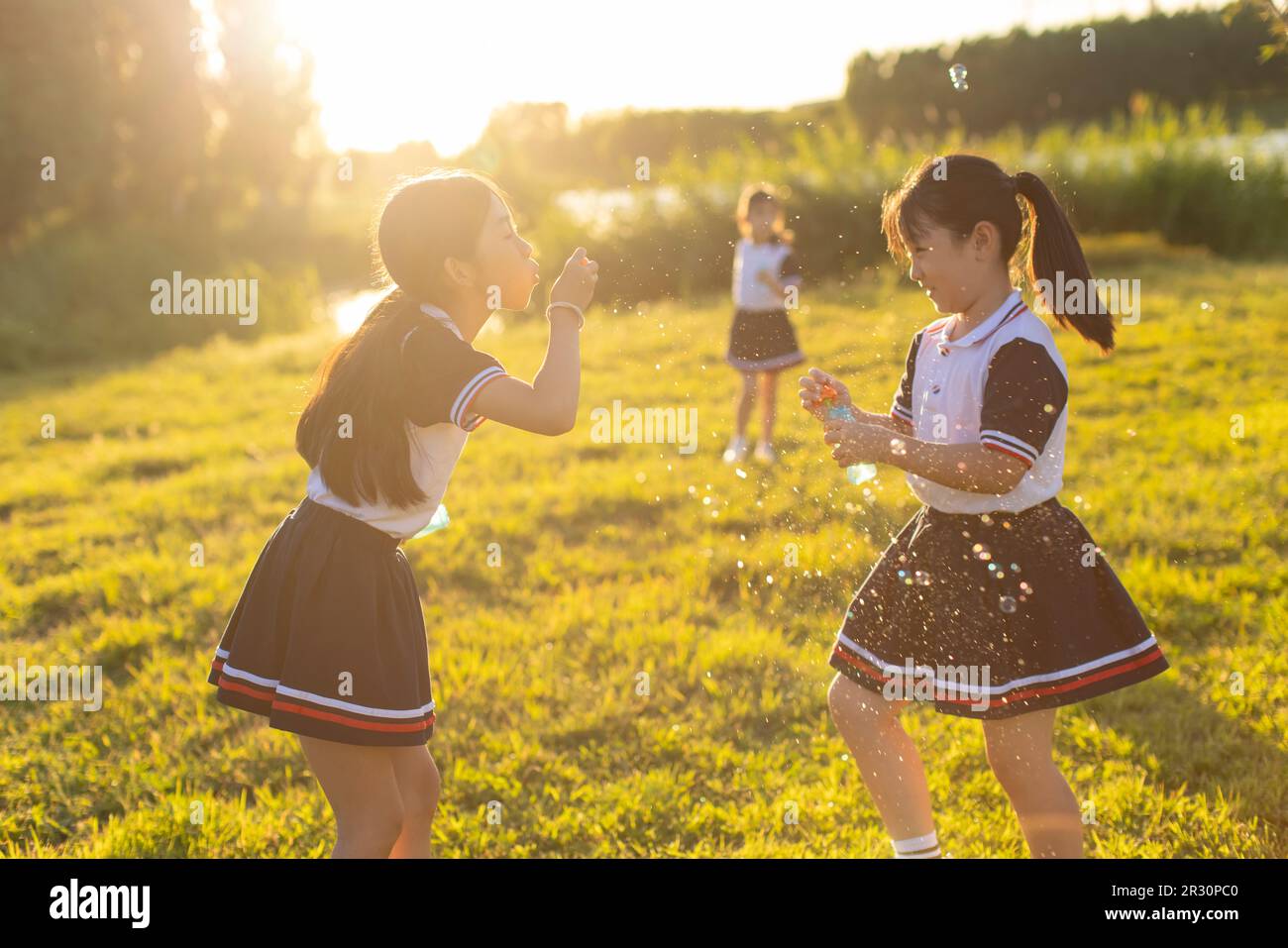 Cheerful Chinese school children blowing bubbles on meadow Stock Photo ...