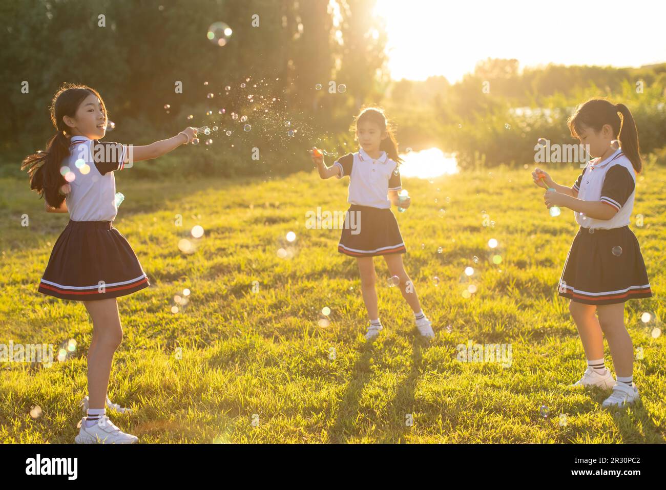 Cheerful Chinese school children blowing bubbles on meadow Stock Photo ...