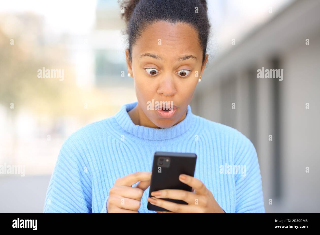 Front view portrait of a surprised black woman using cell phone in the street Stock Photo - Alamy