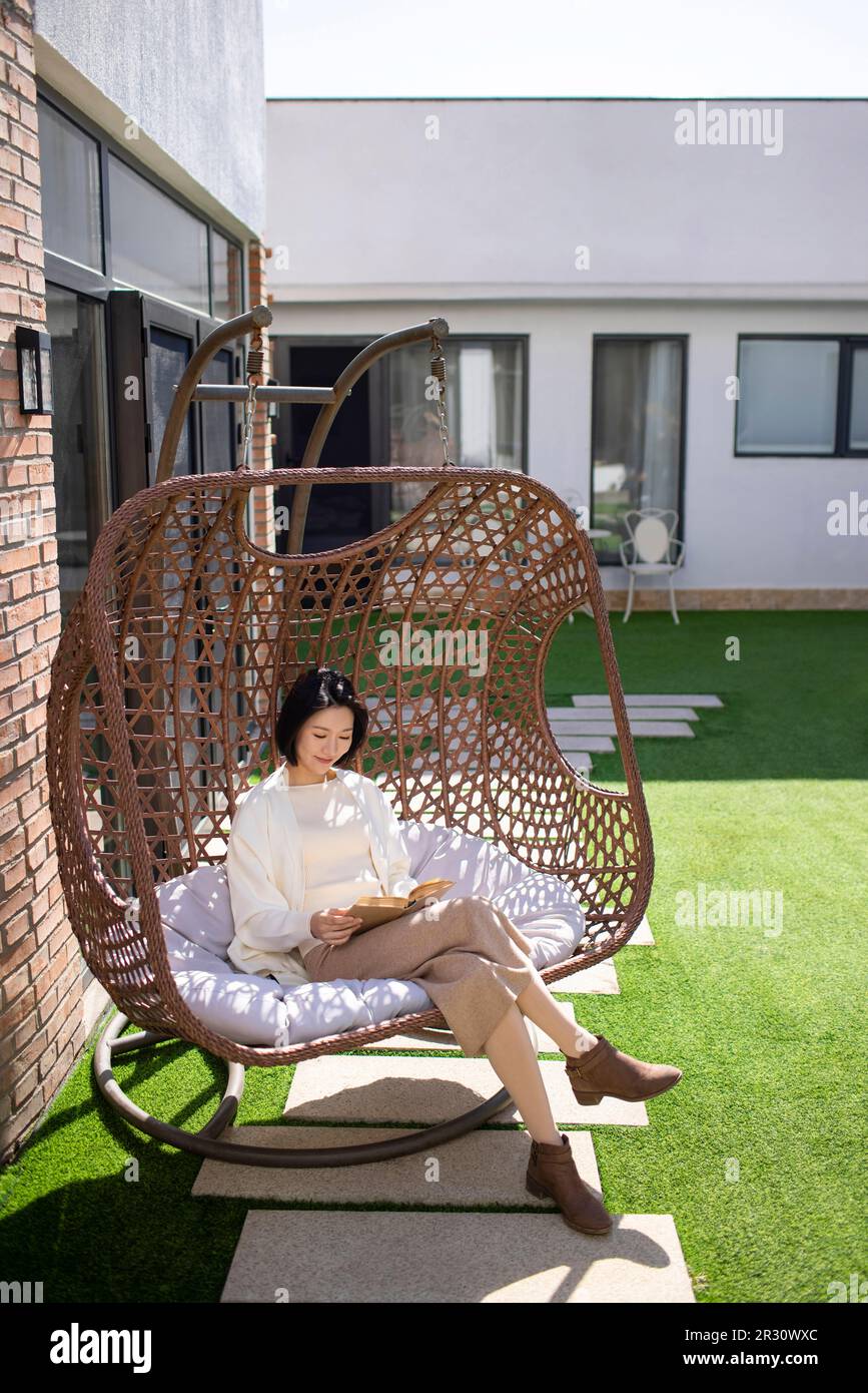 Happy young Chinese woman reading on hanging-chair Stock Photo - Alamy