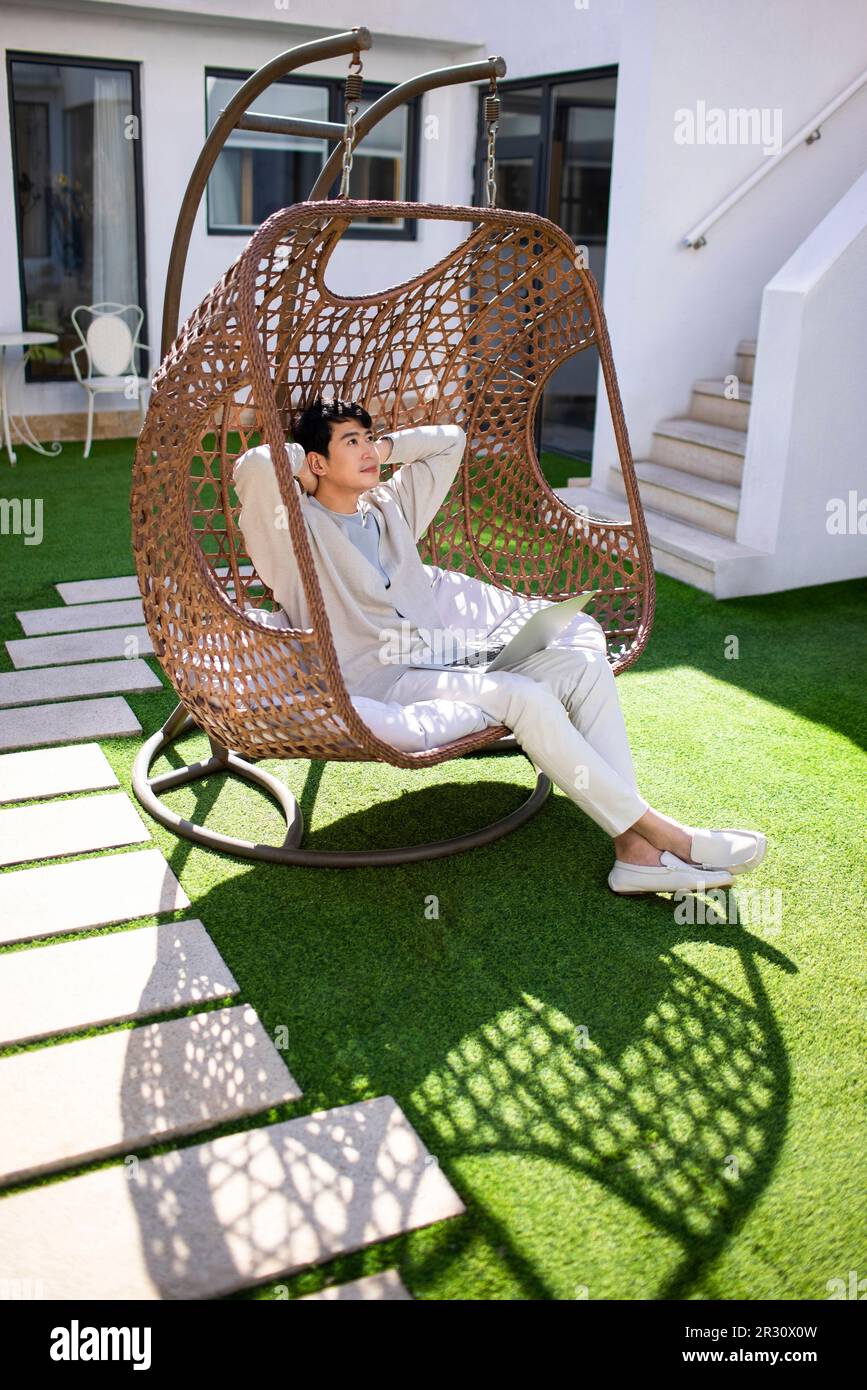 Happy mid adult Chinese man relaxing on hanging-chair Stock Photo - Alamy