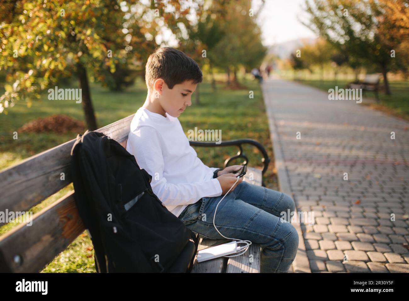 Teenage boy in white shirt use powerbank for charging his smartphone ...