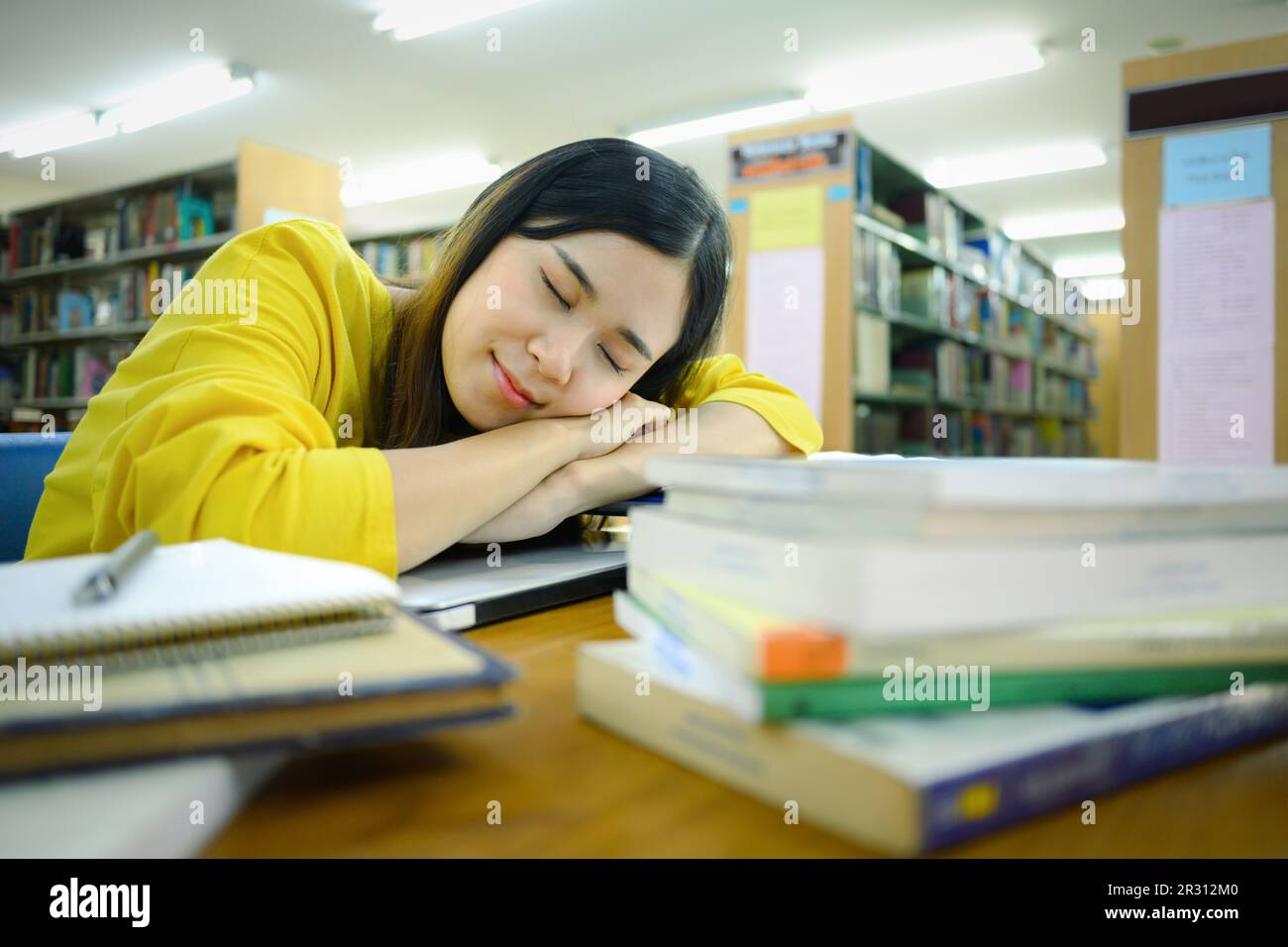 Tired college student sleeping on pile of books in the library with ...