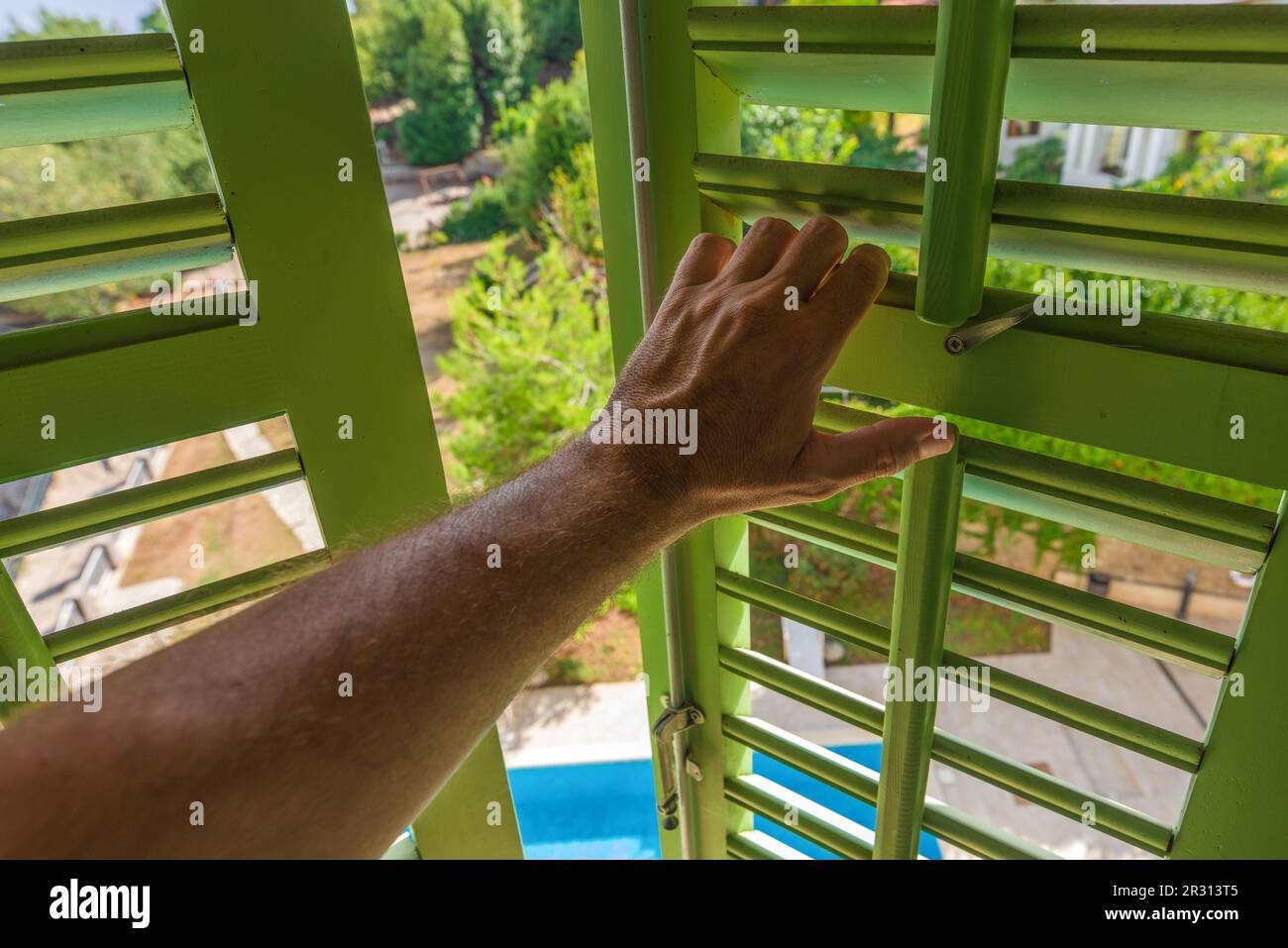 Male hand opening green wooden window shutters at seaside tourist ...