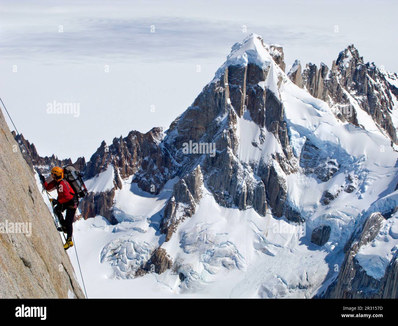 A climber climbs the steep north face of Torre Egger, with the peaks of ...