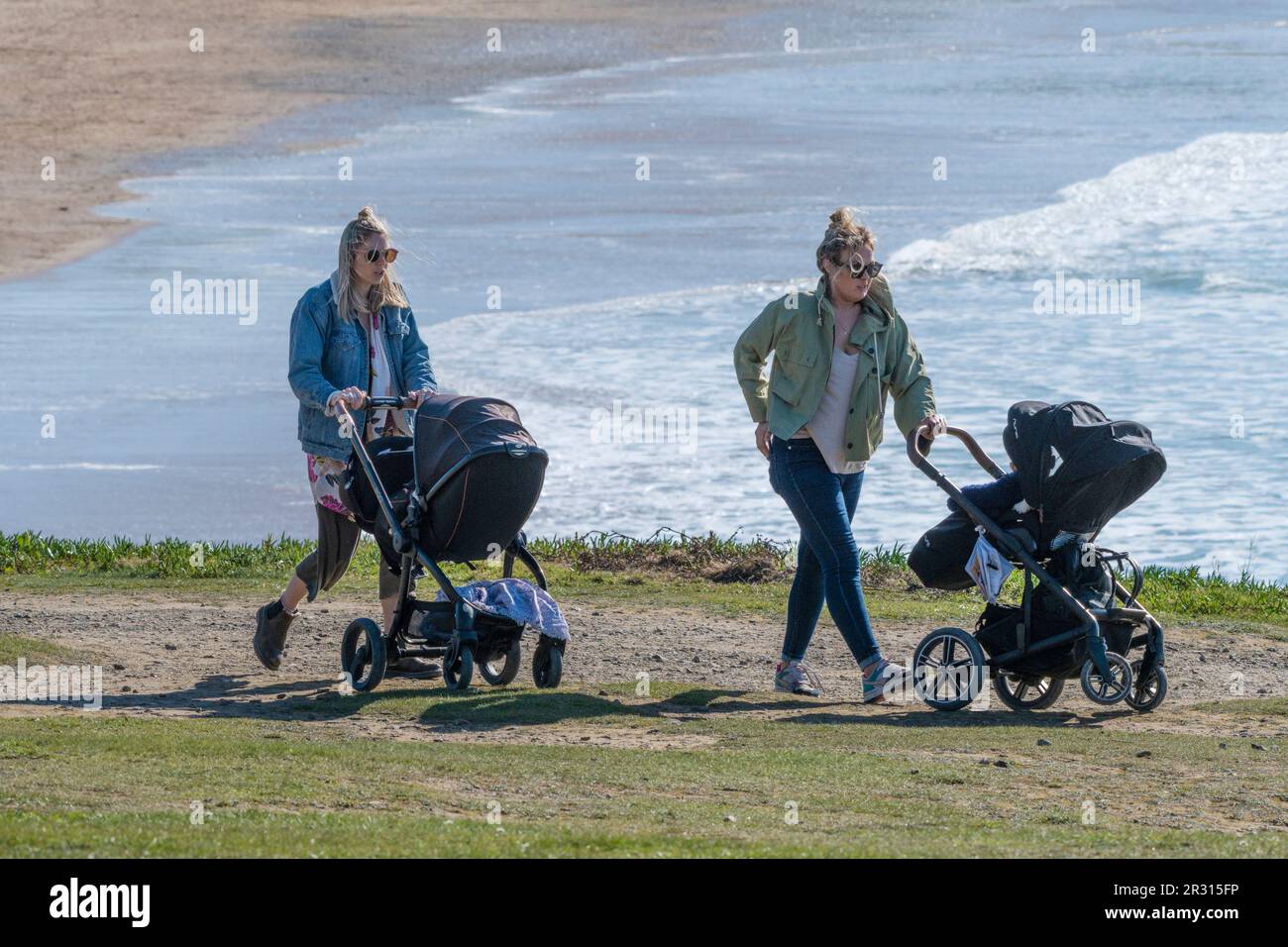 Two young mums pushing their strollers pushchairs on the coast path at ...
