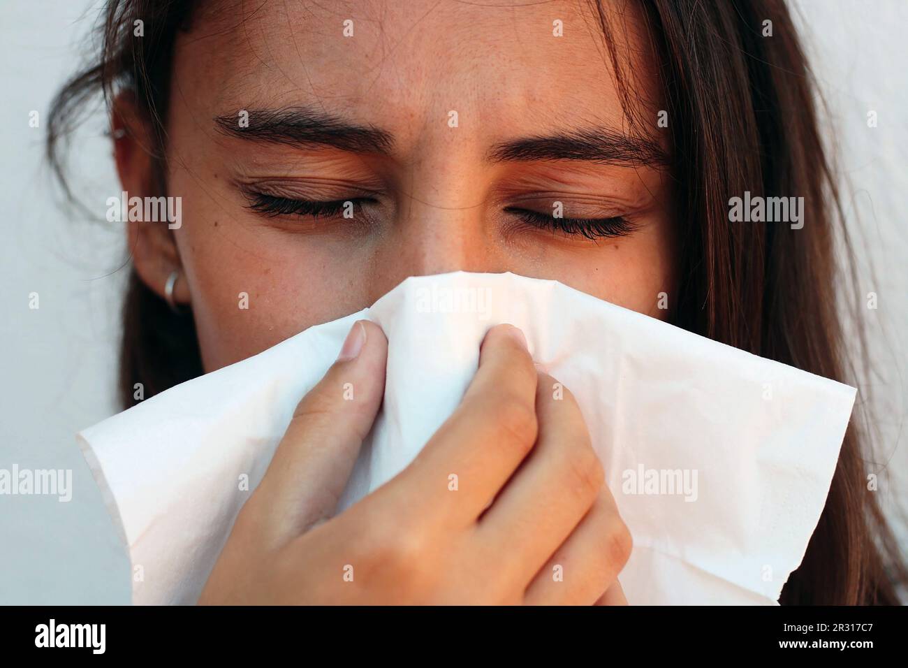 Health and medicine concept - Young woman blowing nose into tissue ...