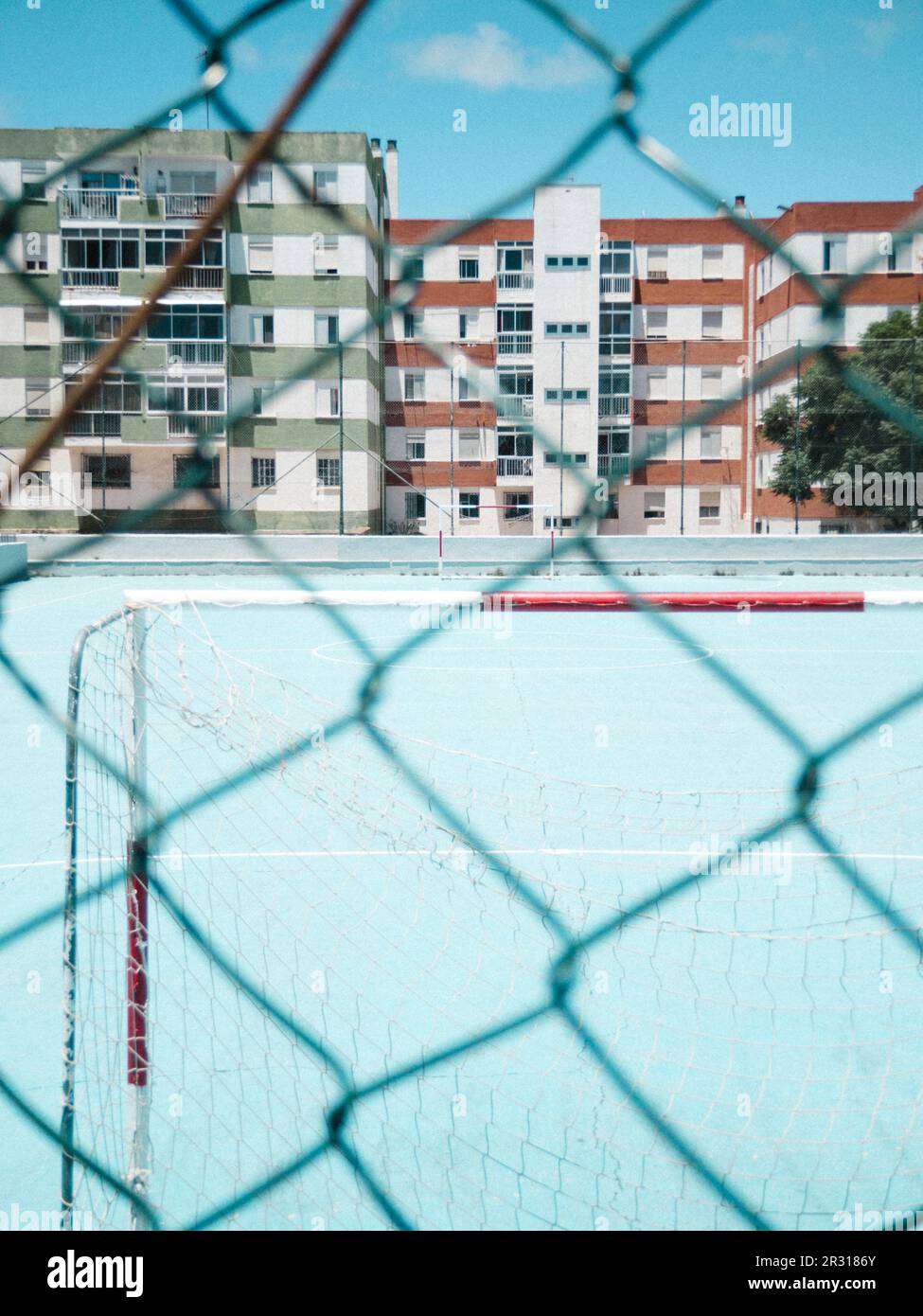 Football goal on blue court across fence with buildings in background ...