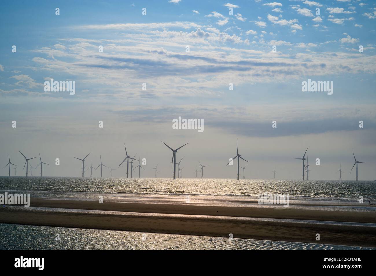 Fans of wind turbines spin over the sparkling sea. Blue sky and white ...