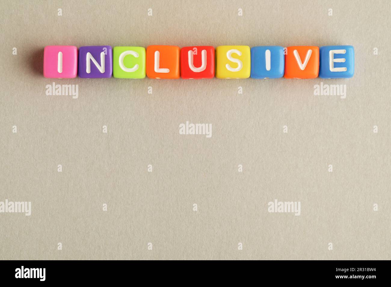 Colorful cubes with word Inclusive on beige background, flat lay. Space ...