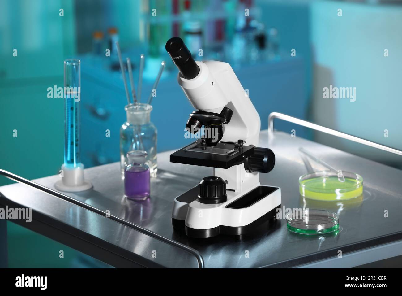 Modern microscope and glassware with colorful liquids on metal table in ...