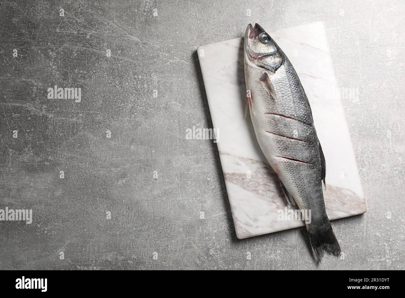 Fresh raw sea bass fish on light gray table, top view. Space for text ...