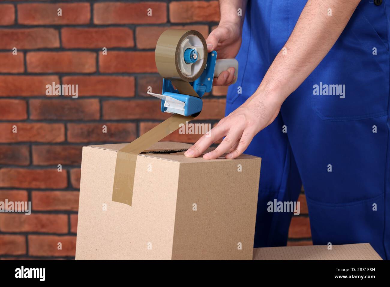 Worker taping box with adhesive tape dispenser near brick wall, closeup ...