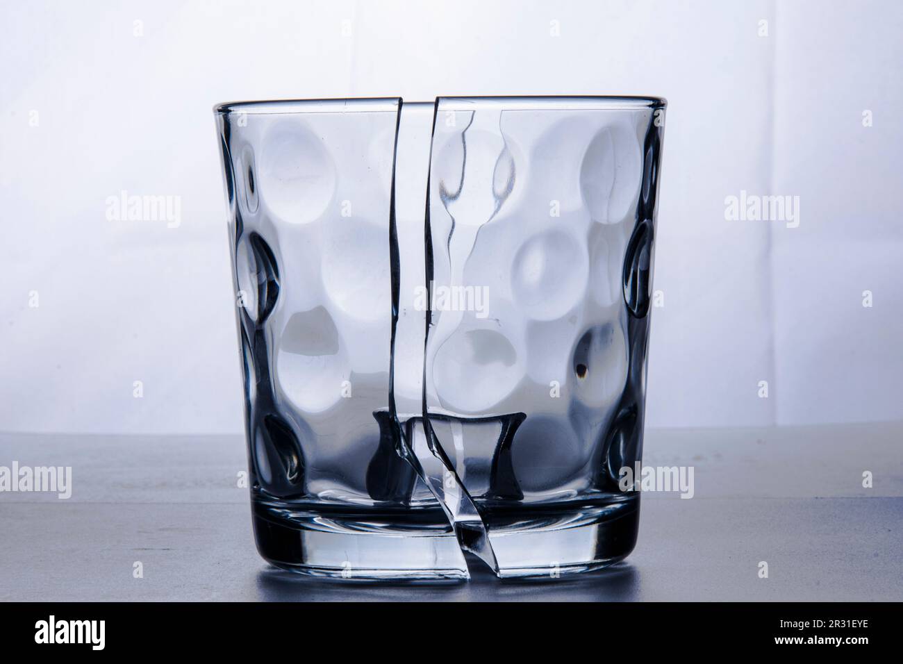 Glass broken in two halves with an ice cube. Photographed on white ...