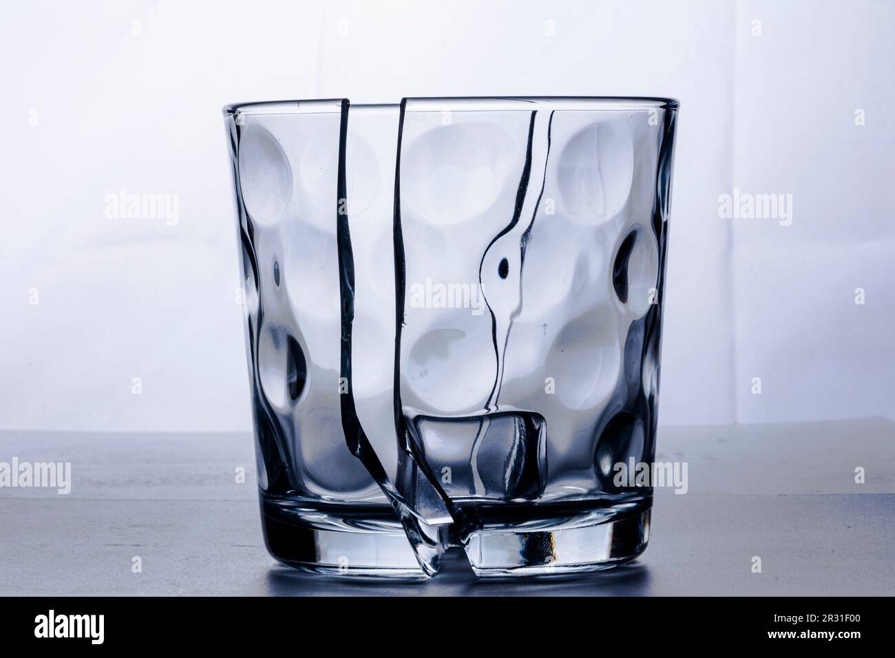 Glass broken in two halves with an ice cube. Photographed on white ...