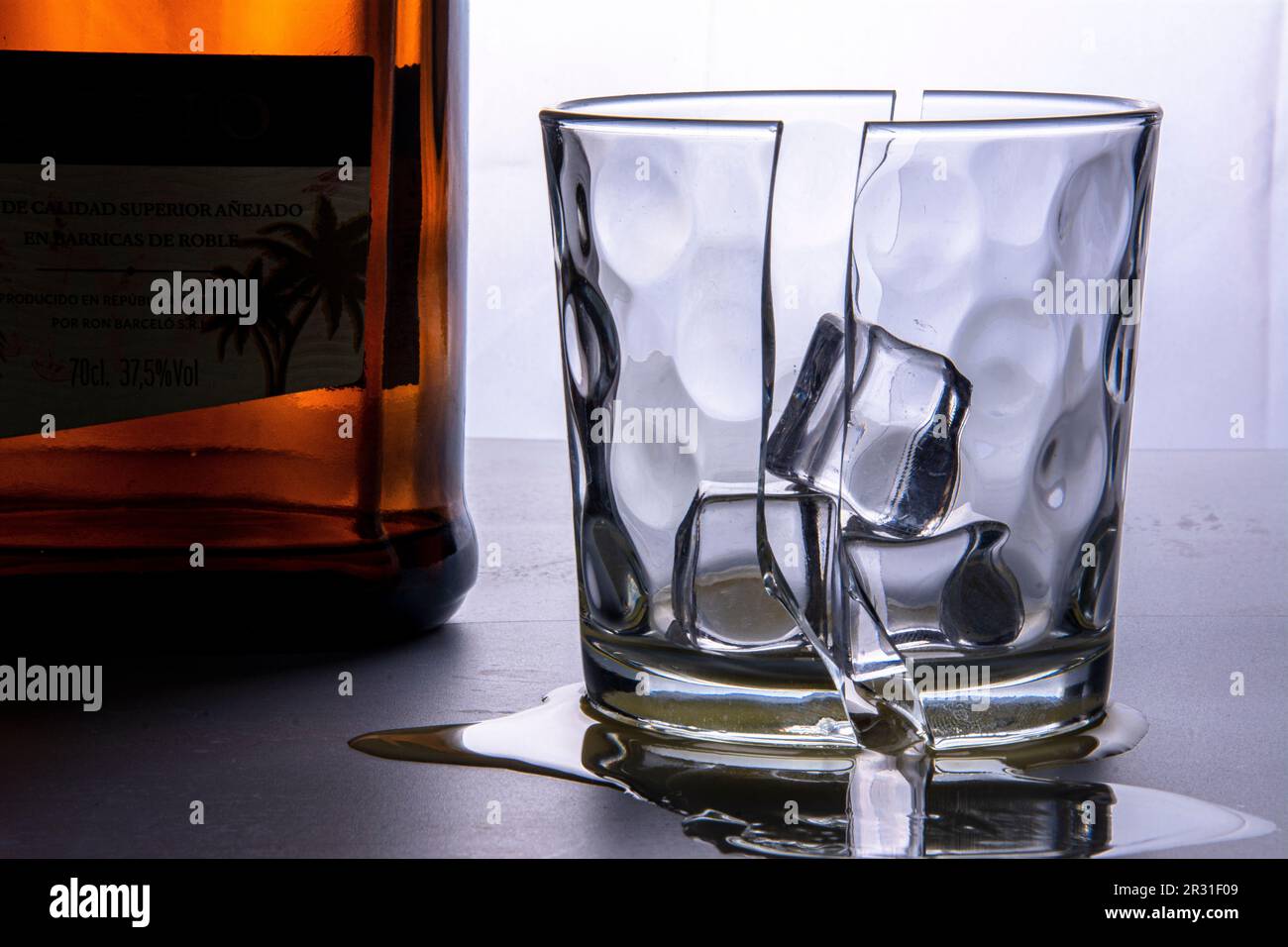 Empty rum bottle and broken glass in two halves with three ice cubes ...