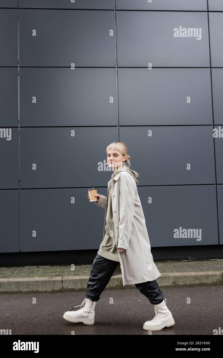Full Length Of Trendy Woman With Blonde Hair With Bangs Walking In Coat