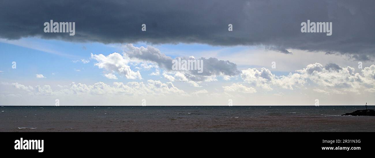 rain falling from storm clouds above a dark sea with blue sky in the ...